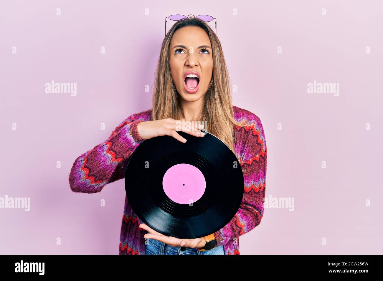 Beautiful hispanic woman wearing hippie style holding vinyl disc angry ...