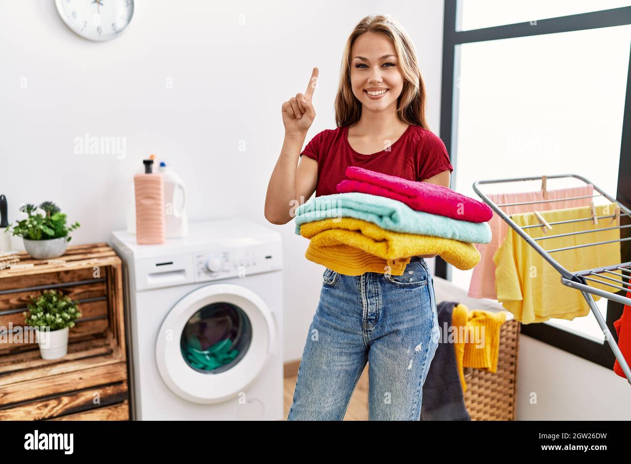 Young caucasian woman holding clean laundry smiling with an idea or ...