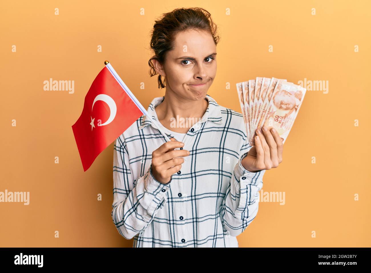 Young brunette woman holding turkey flag and liras banknotes skeptic ...