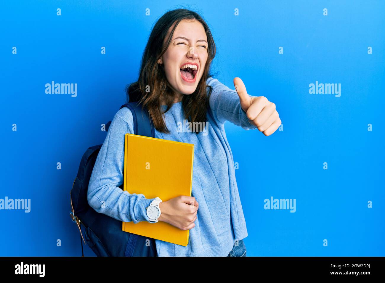 Young brunette student woman wearing student backpack doing thumbs up ...