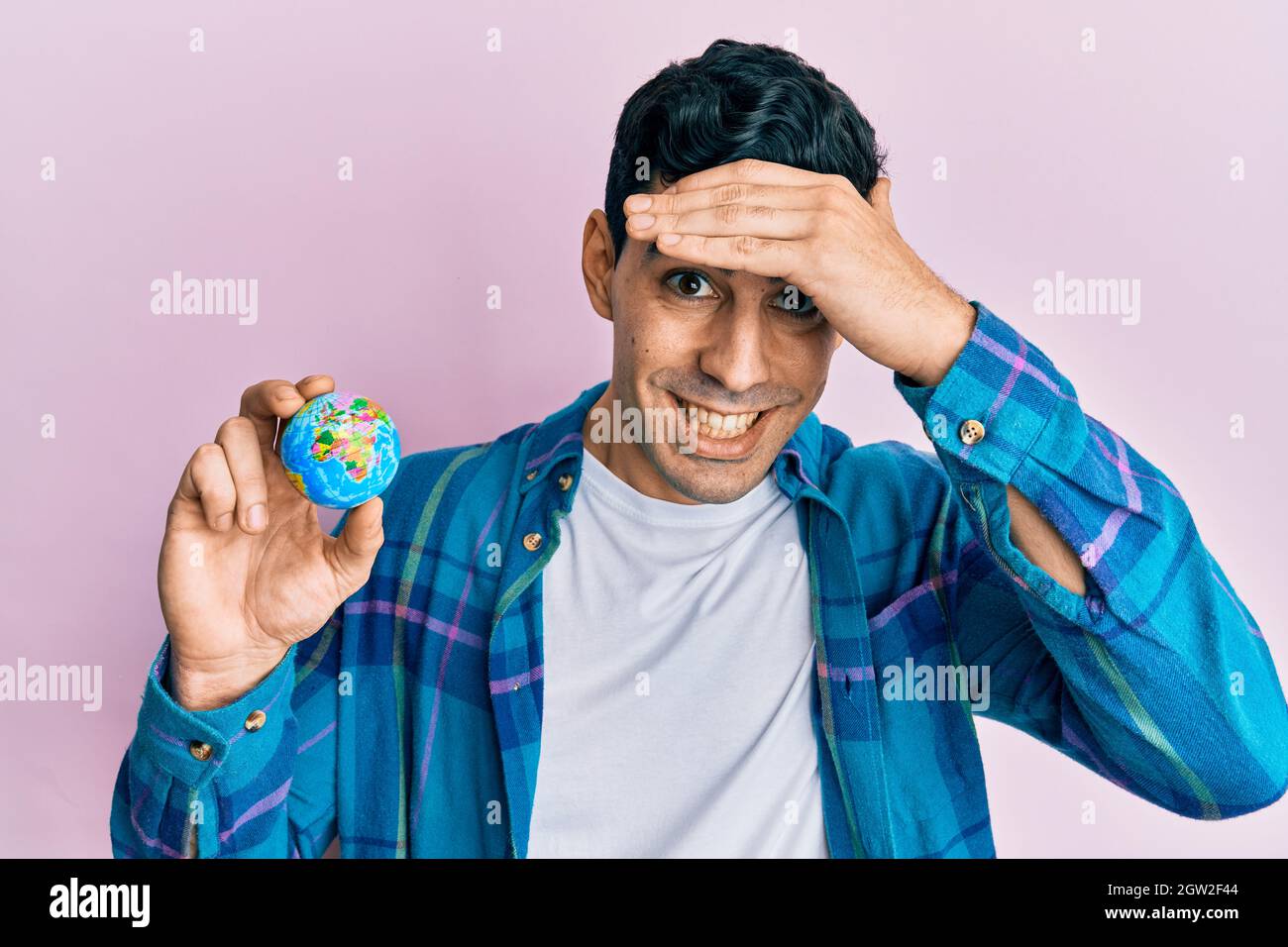 Handsome hispanic man holding small world ball stressed and frustrated ...