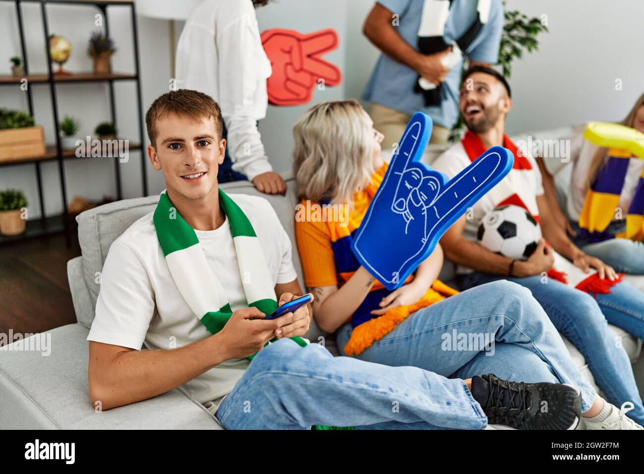Group of young friends watching and supporting soccer match. Man using ...