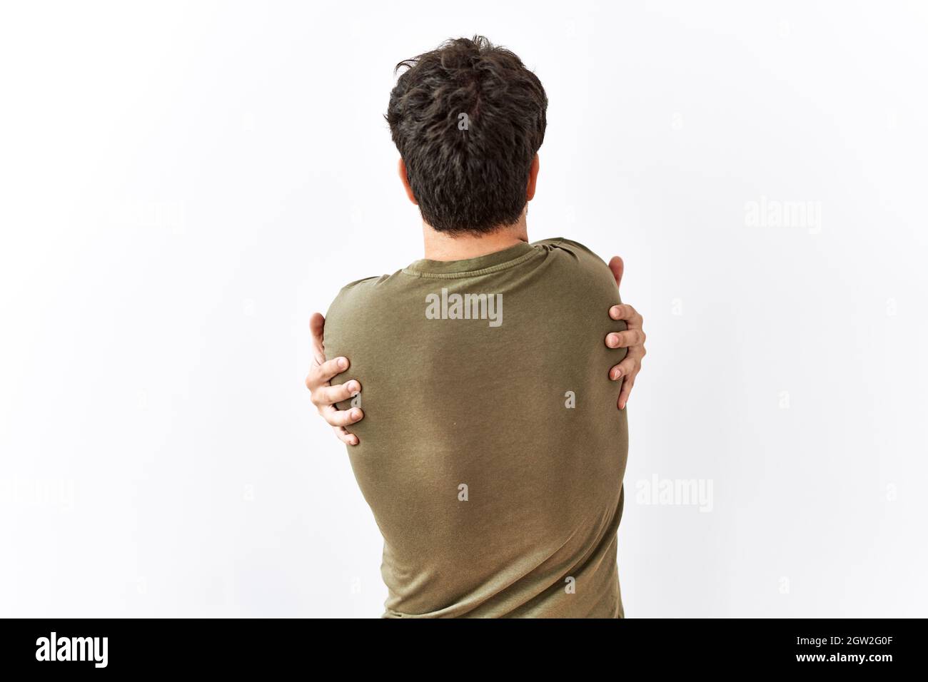 Hispanic man standing over isolated white background hugging oneself ...