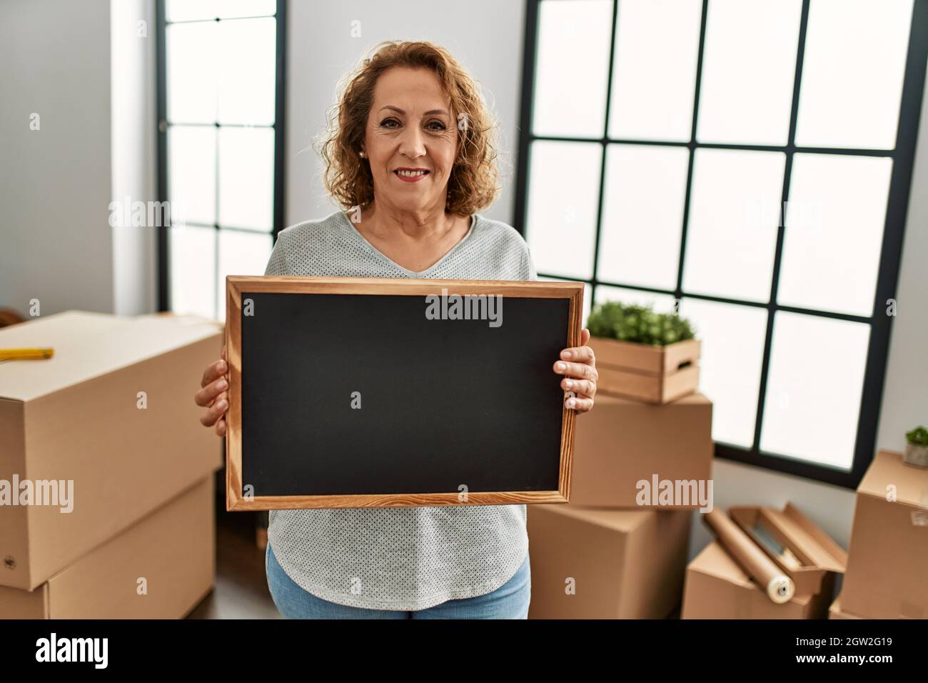 Middle age caucasian woman smiling happy holding empty blackboard at ...