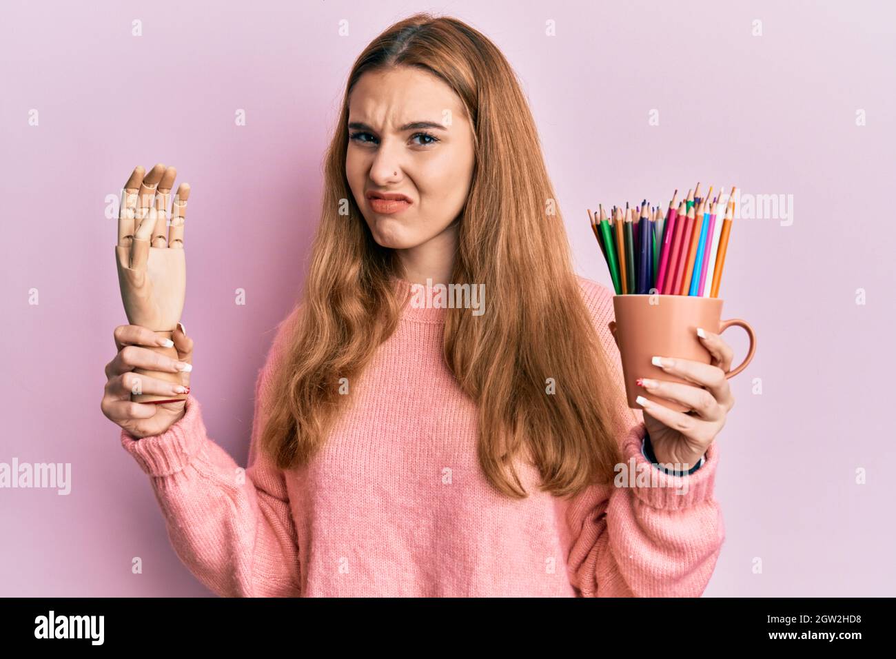 Young blonde woman holding small wooden manikin hand and pencils ...