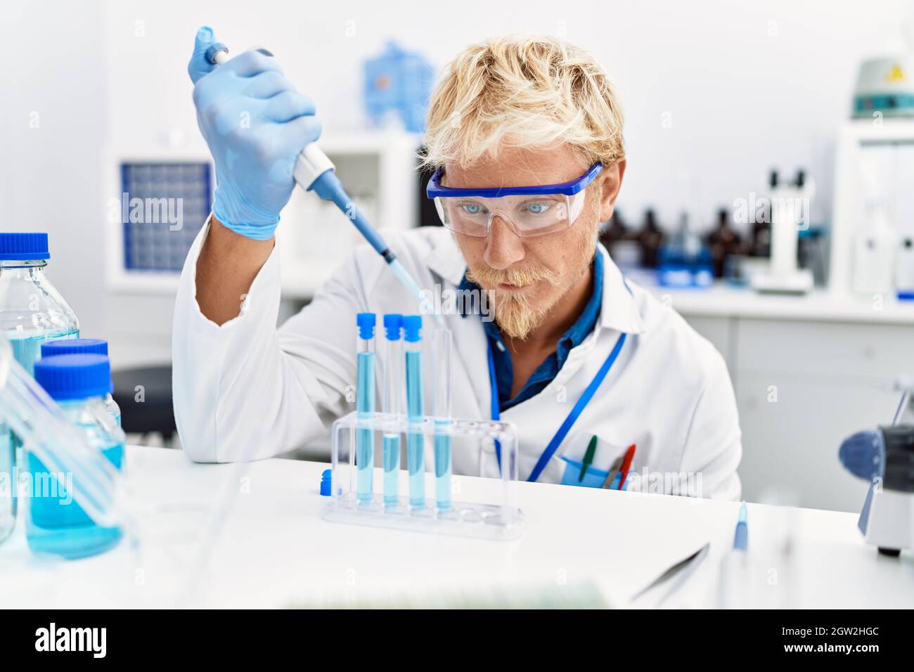 Young caucasian man wearing scientist uniform using pipette at ...