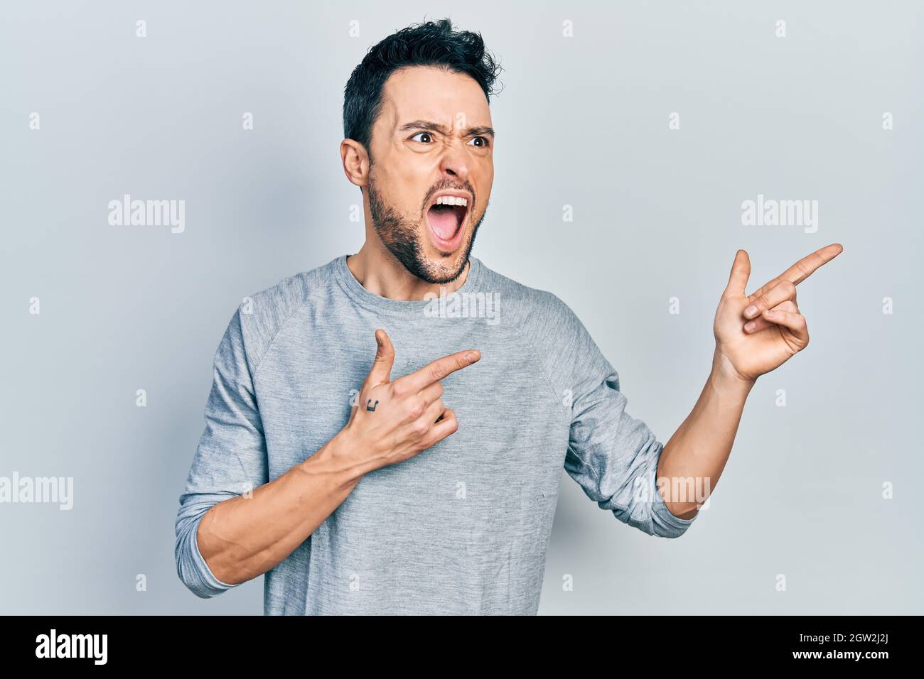Young hispanic man pointing with fingers to the side angry and mad ...