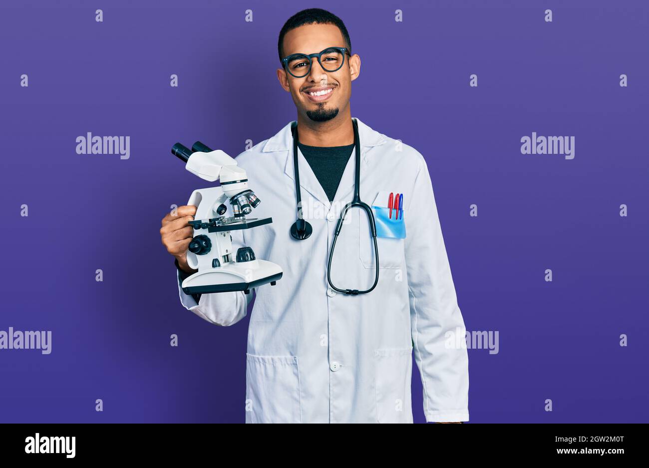 Young african american man wearing scientist uniform holding microscope ...