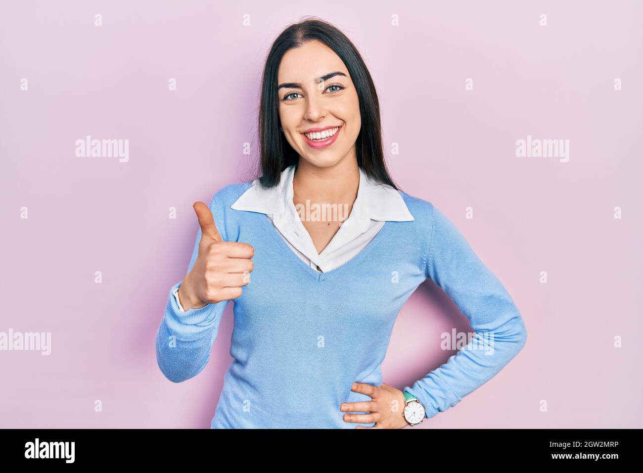 Beautiful woman with blue eyes standing over pink background doing ...