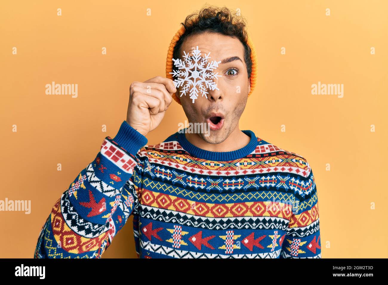 Young handsome man holding snowflake wearing winter sweater scared and ...