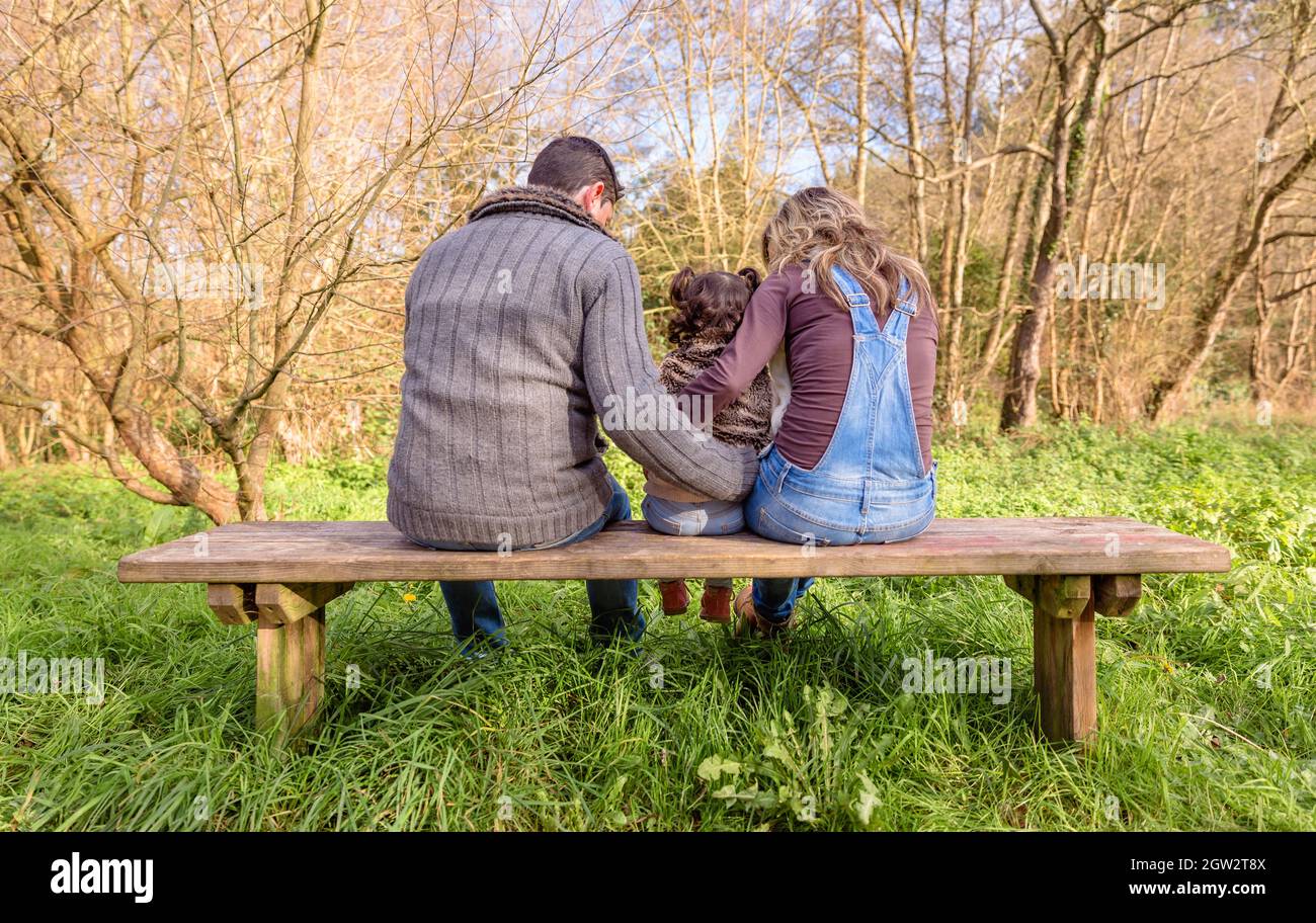 Rear View Of Daughter Sitting Between Parents On Bench In Forest Stock ...