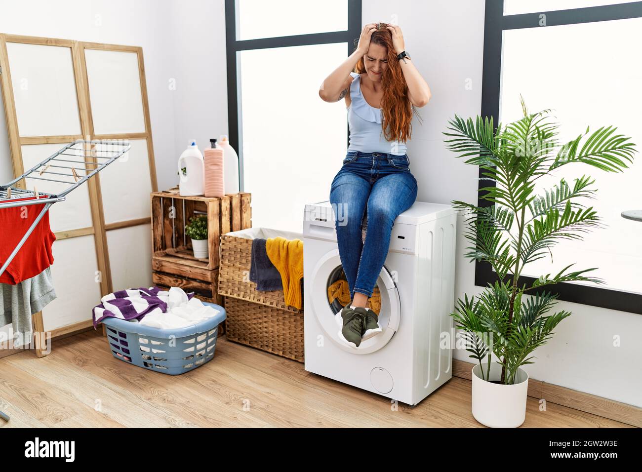 Young redhead woman doing laundry sitting on washing machine suffering ...