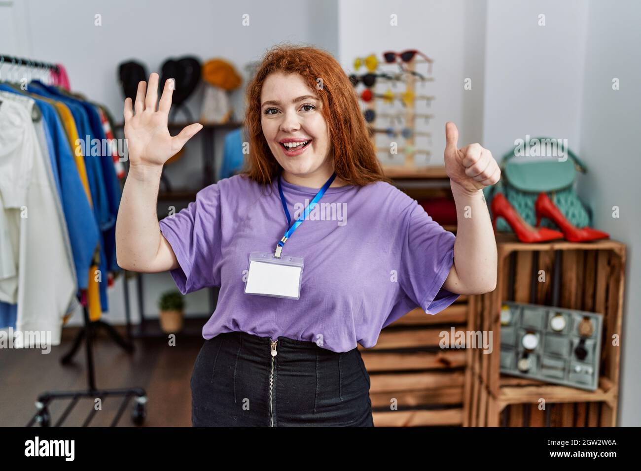 Young redhead woman working as manager at retail boutique showing and pointing up with fingers ...