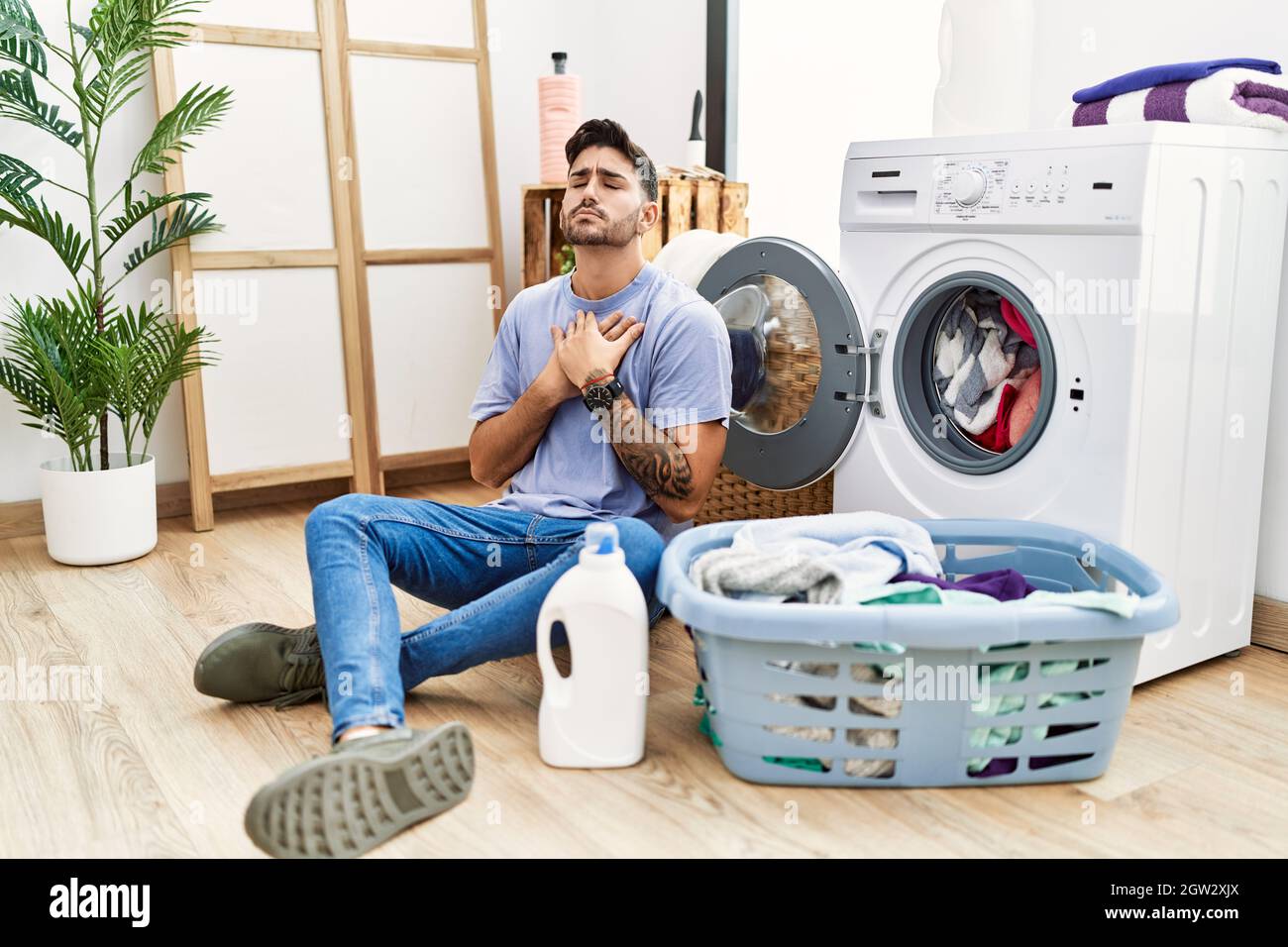 Young hispanic man putting dirty laundry into washing machine smiling ...