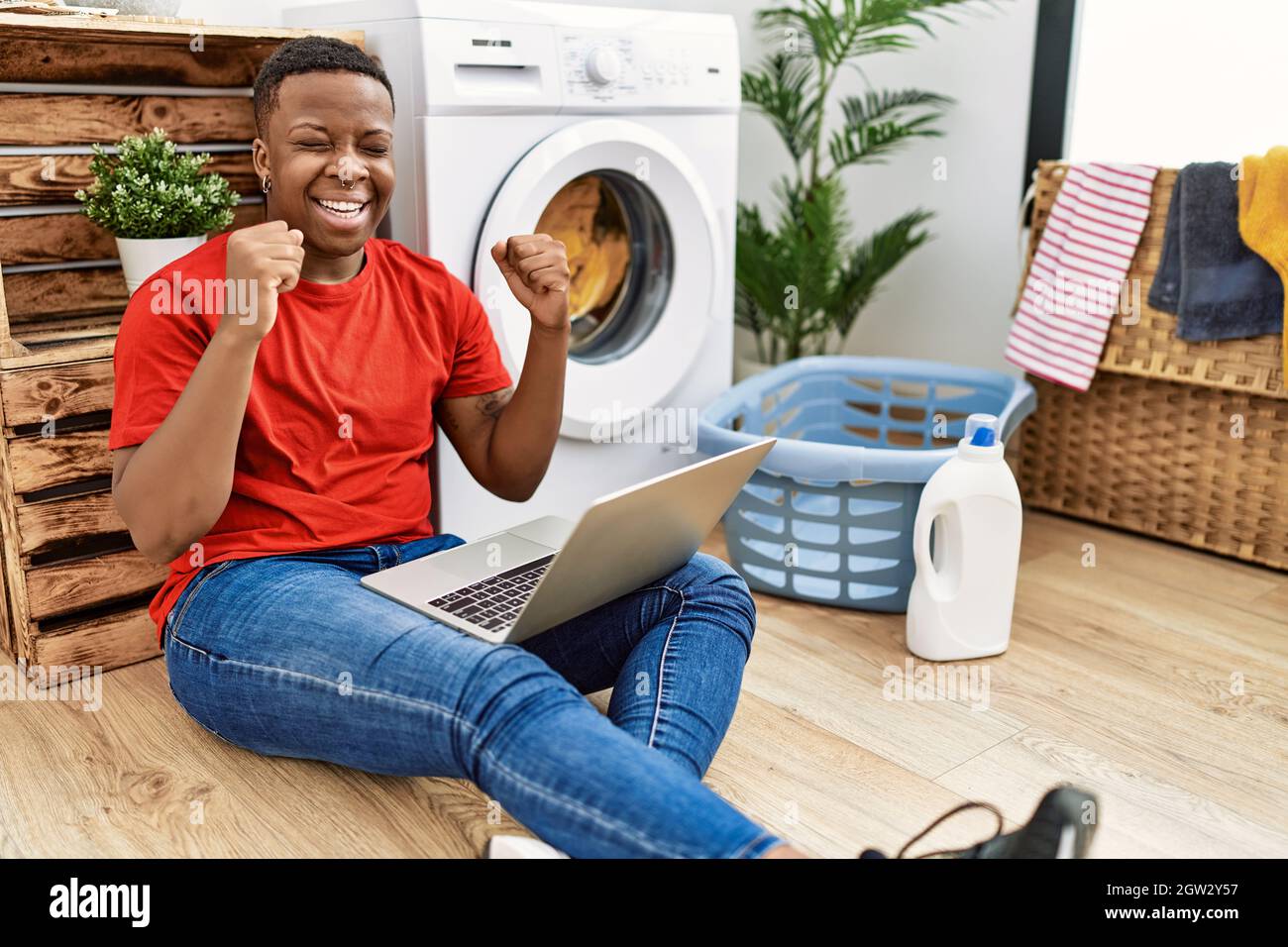 Young african man doing laundry and using computer excited for success ...