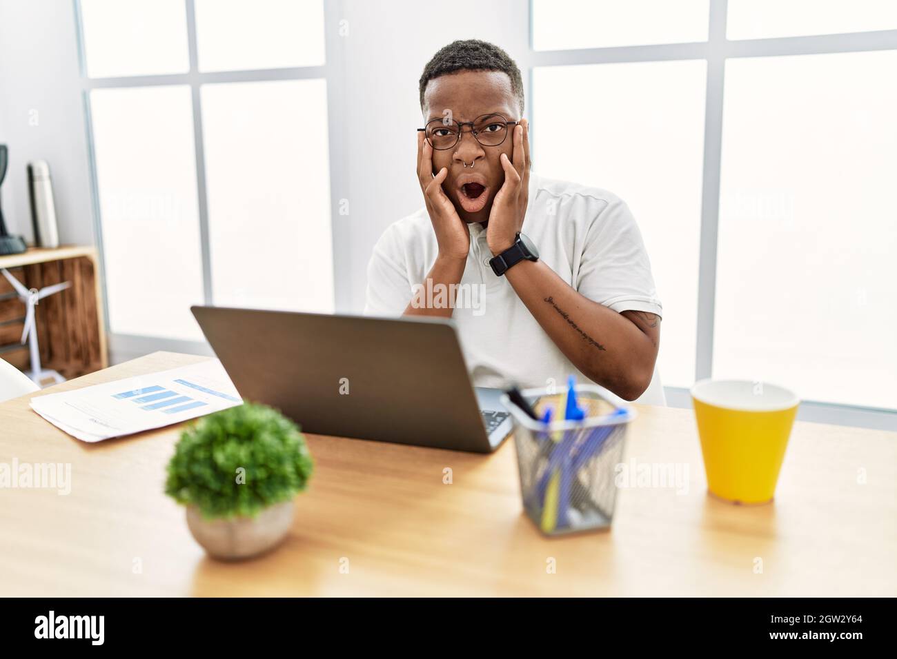 Young african man working at the office using computer laptop afraid ...