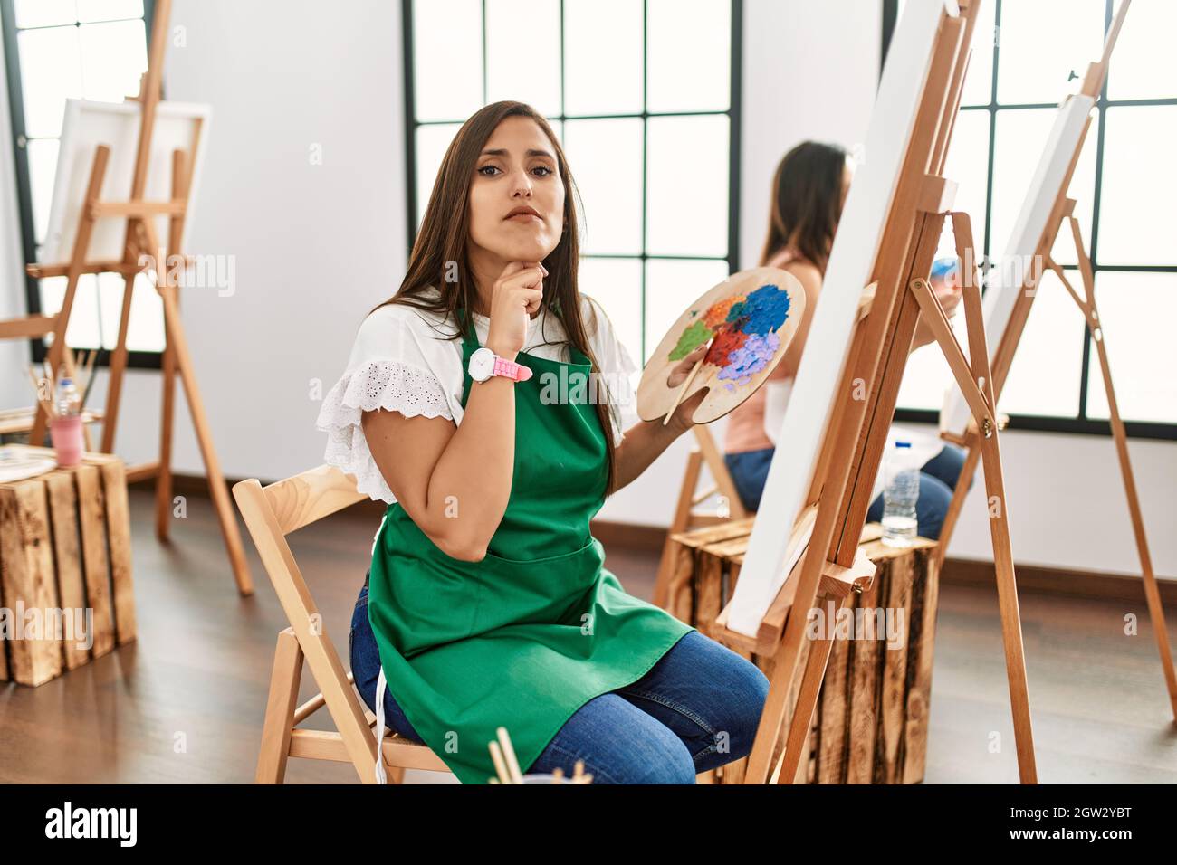Young hispanic artist women painting on canvas at art studio touching ...