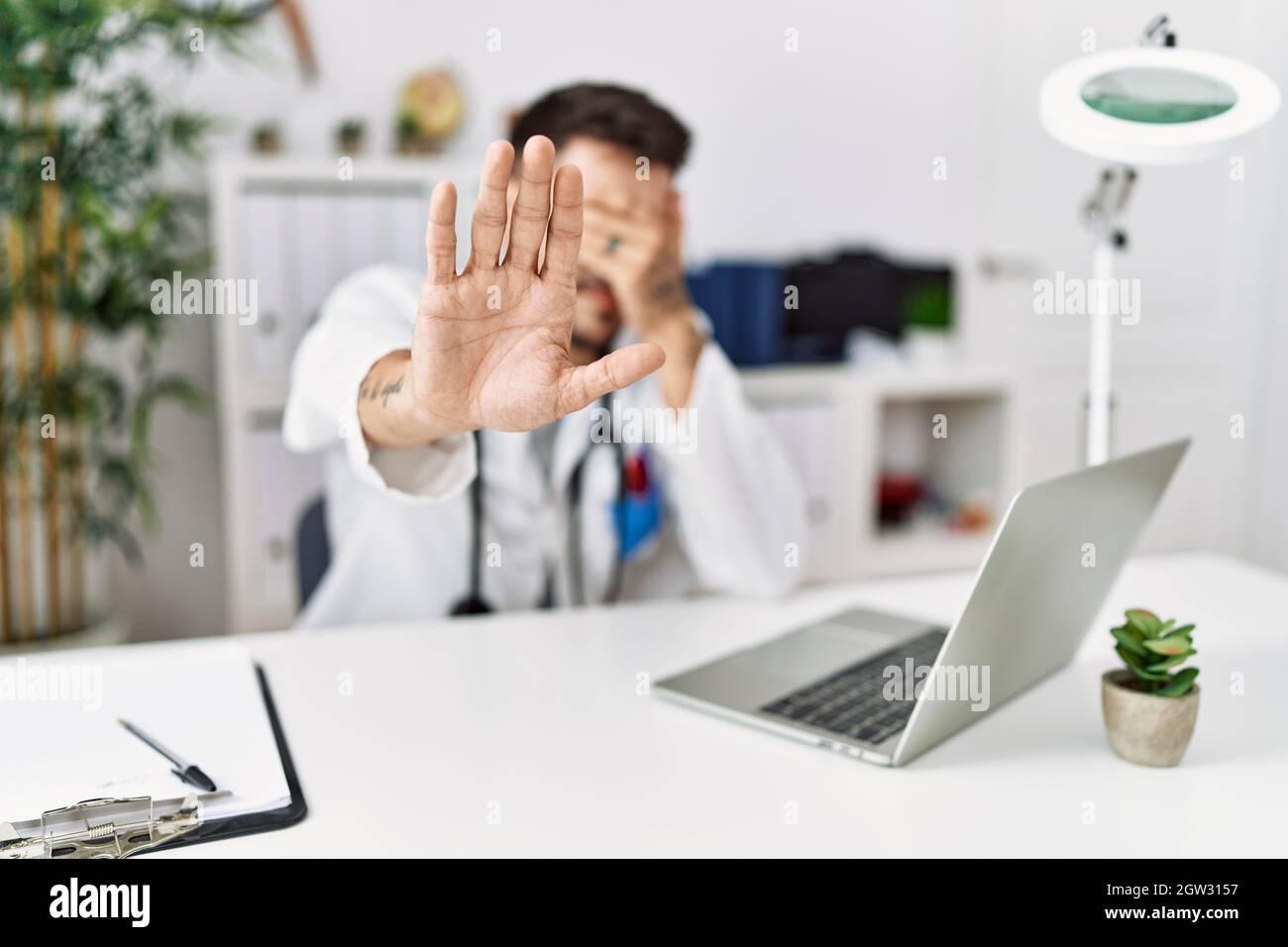 Young doctor working at the clinic using computer laptop covering eyes ...