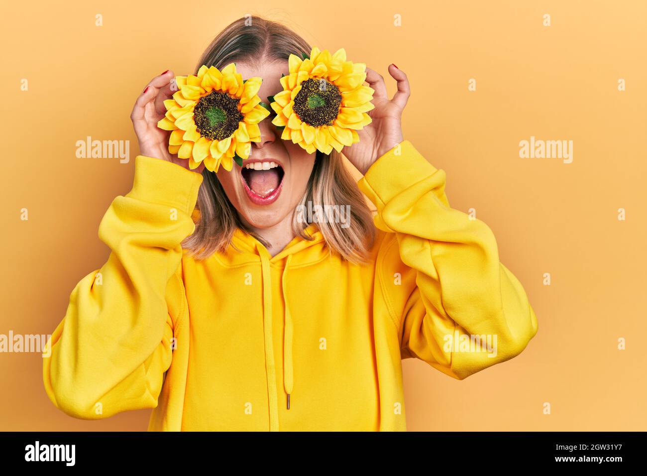 Beautiful caucasian woman holding yellow sunflowers over eyes angry and ...