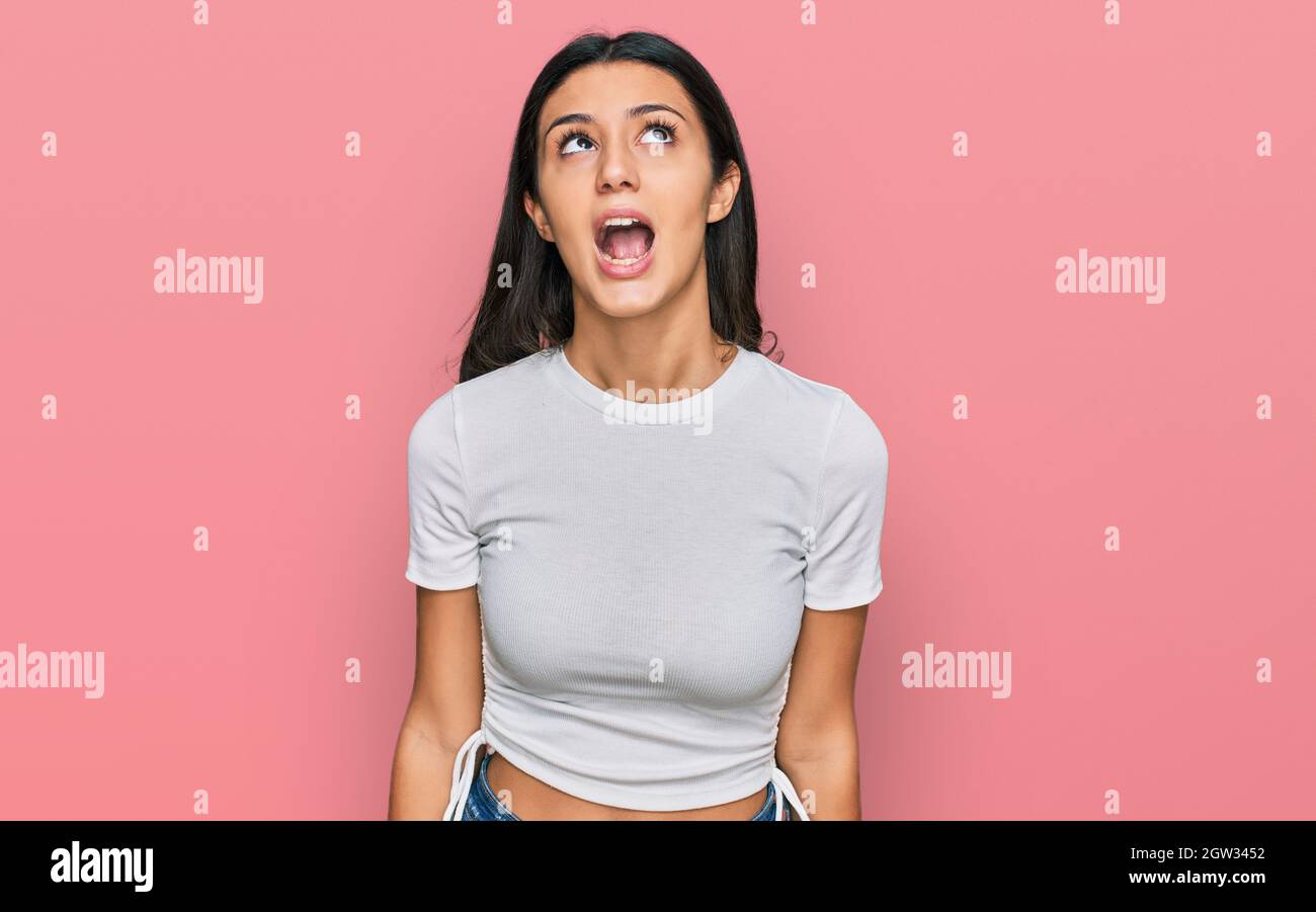 Young hispanic girl wearing casual white t shirt angry and mad screaming frustrated and furious ...