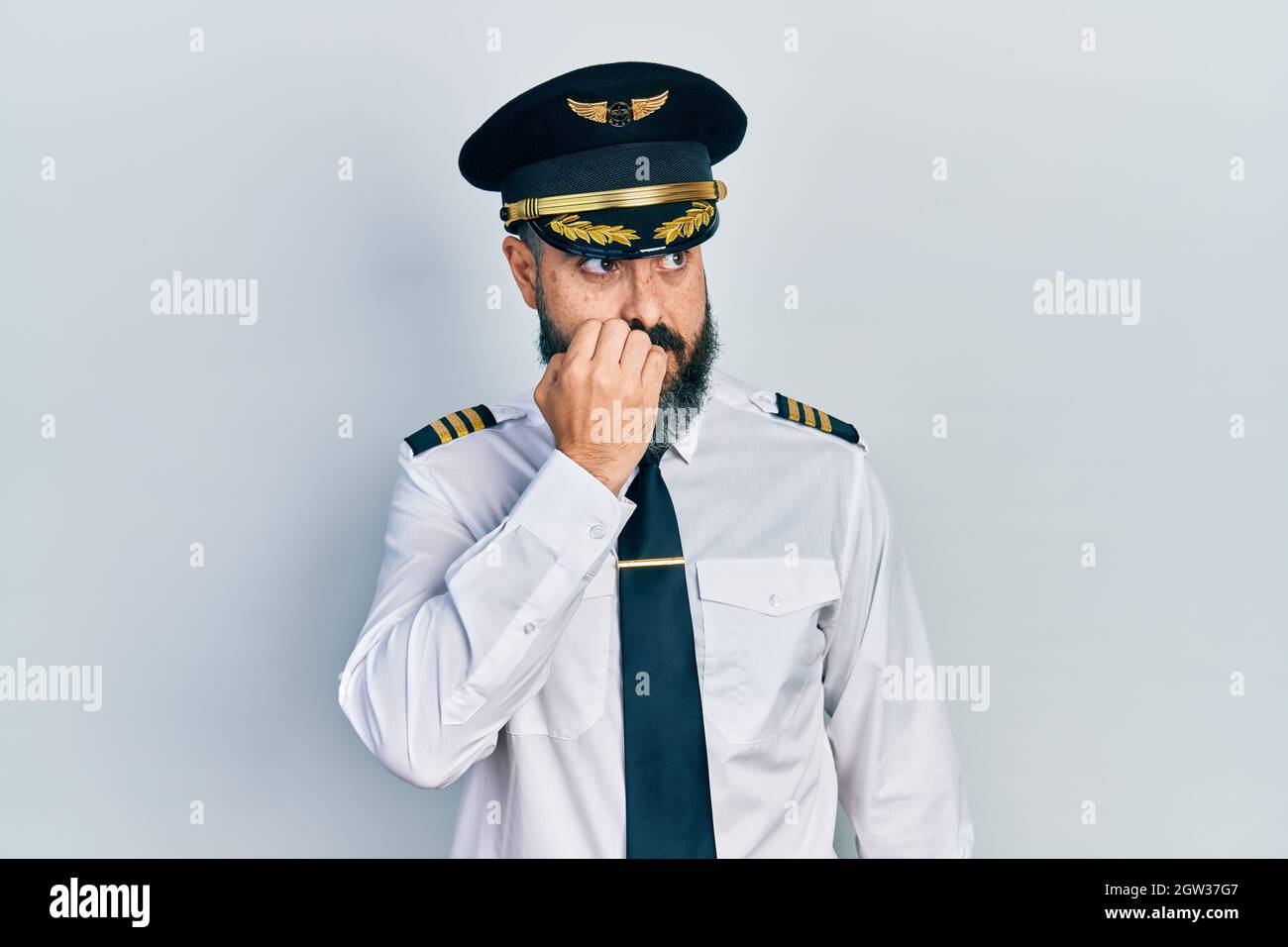 Young hispanic man wearing airplane pilot uniform looking stressed and ...