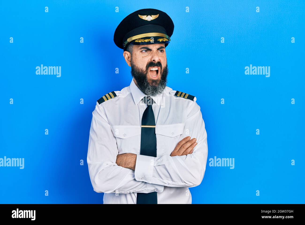 Young hispanic man wearing airplane pilot uniform with arms crossed ...