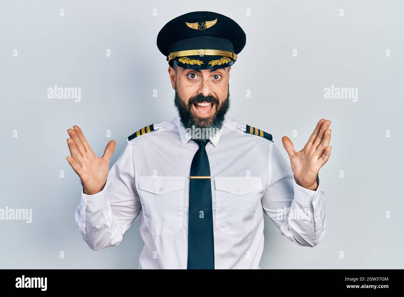 Young hispanic man wearing airplane pilot uniform celebrating crazy and ...