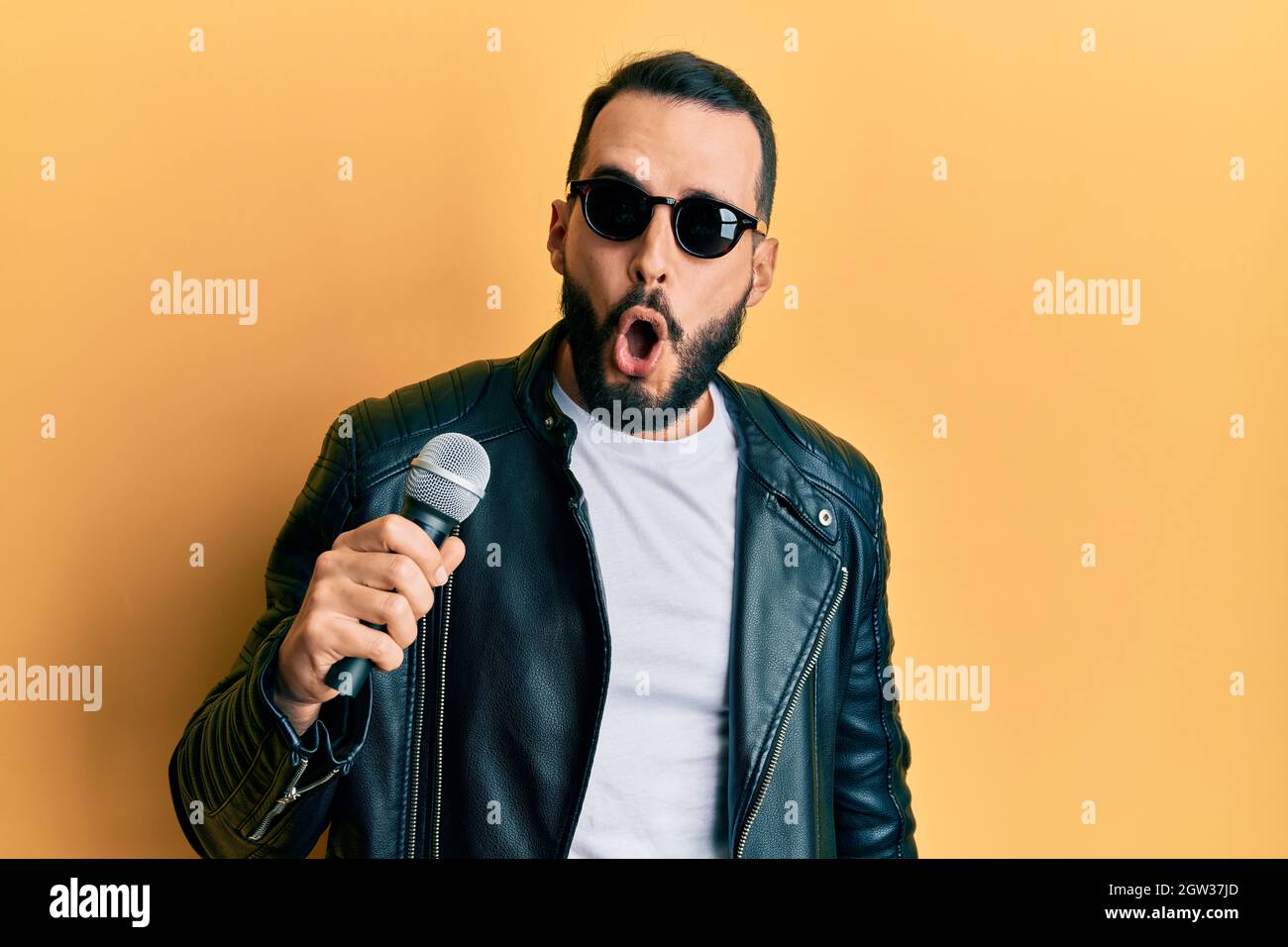 Young man with beard singing song using microphone scared and amazed ...