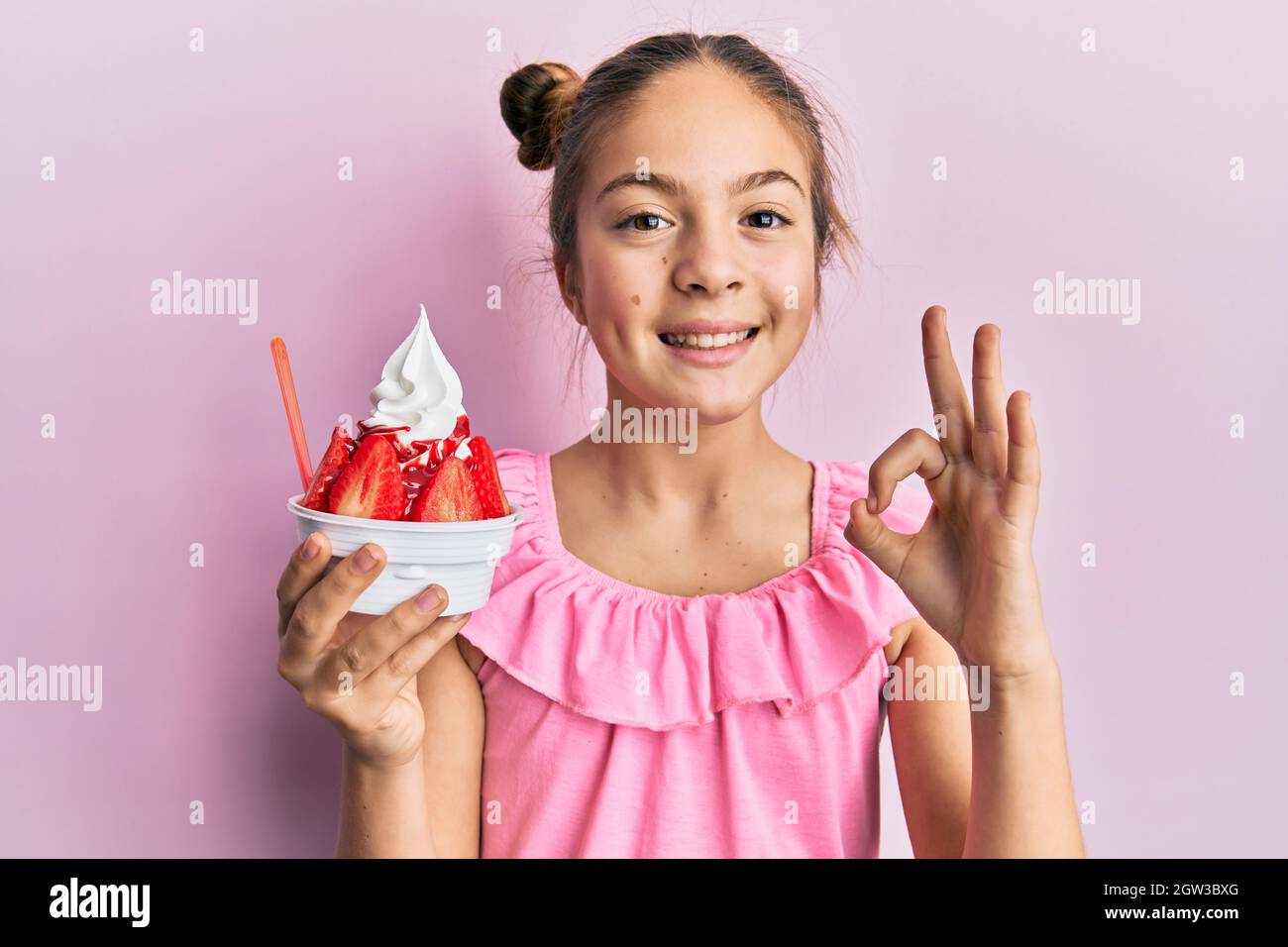 Beautiful brunette little girl eating strawberry ice cream doing ok ...