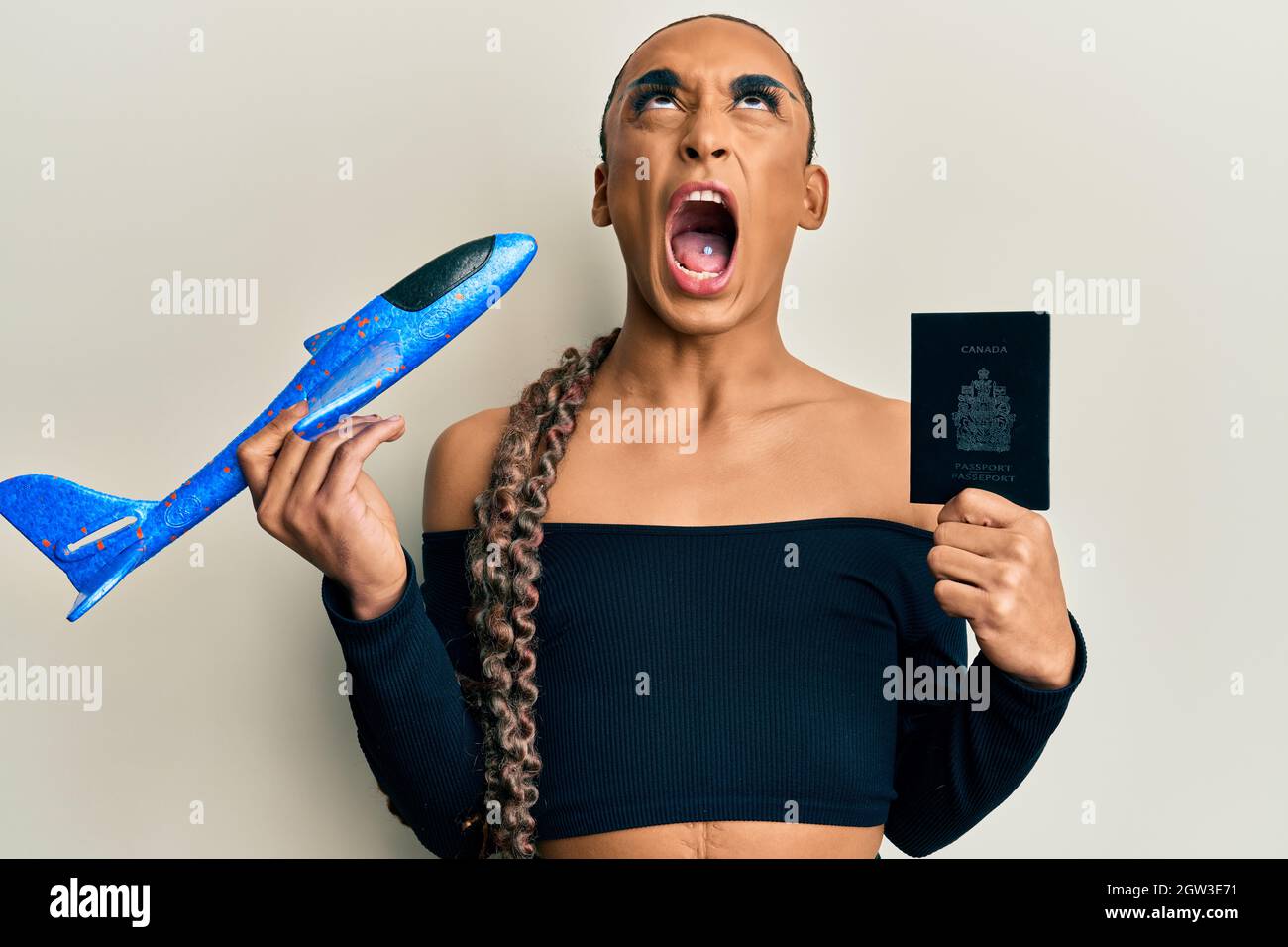 Hispanic man wearing make up and long hair holding paper plane and ...