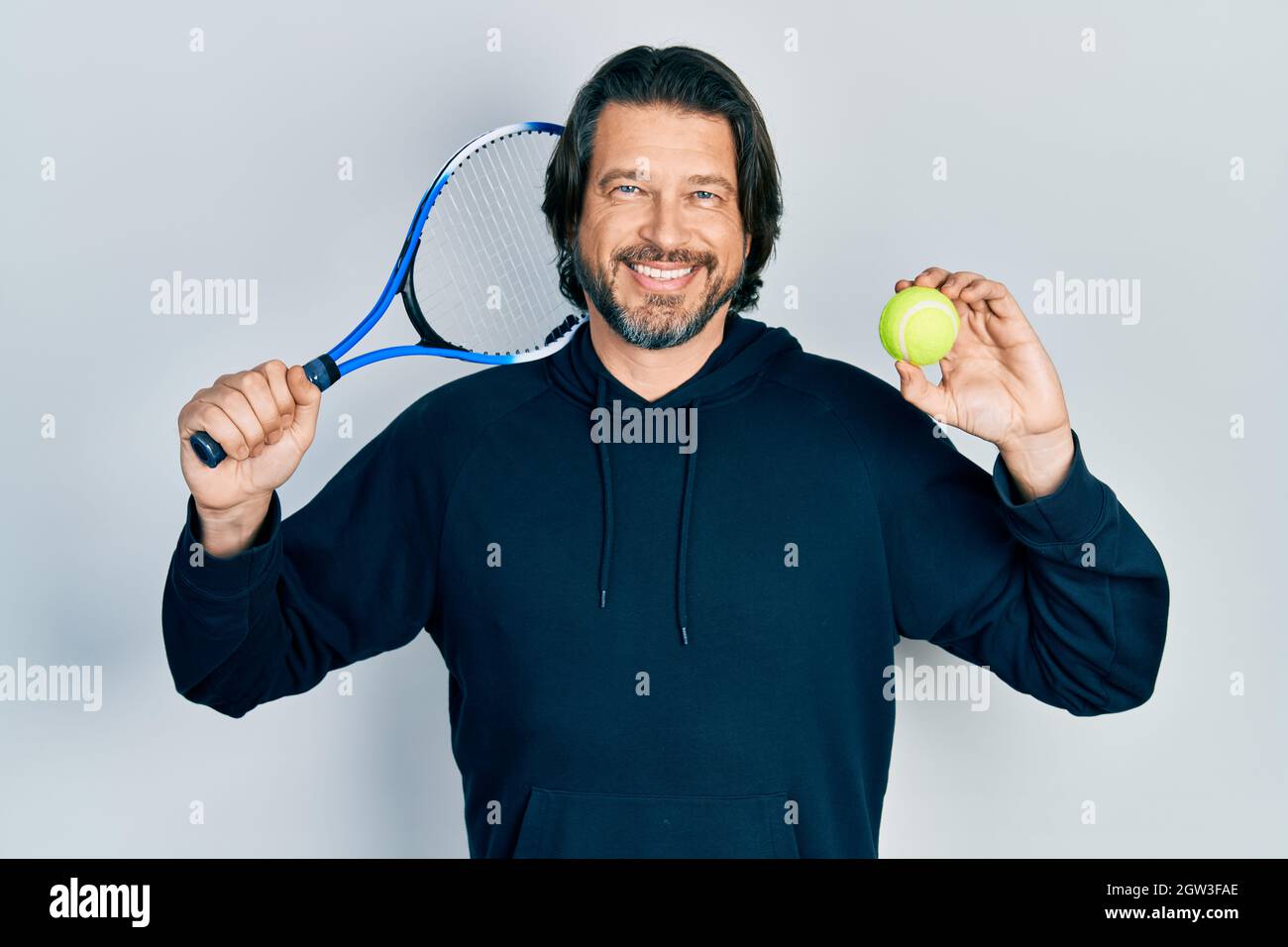 Middle age caucasian man playing tennis holding racket and ball smiling ...