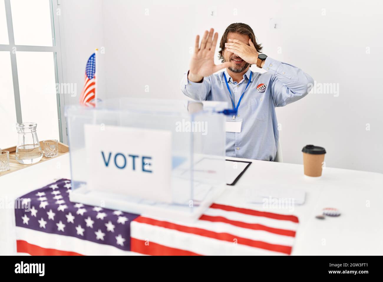 Handsome middle age man sitting at voting stand covering eyes with ...