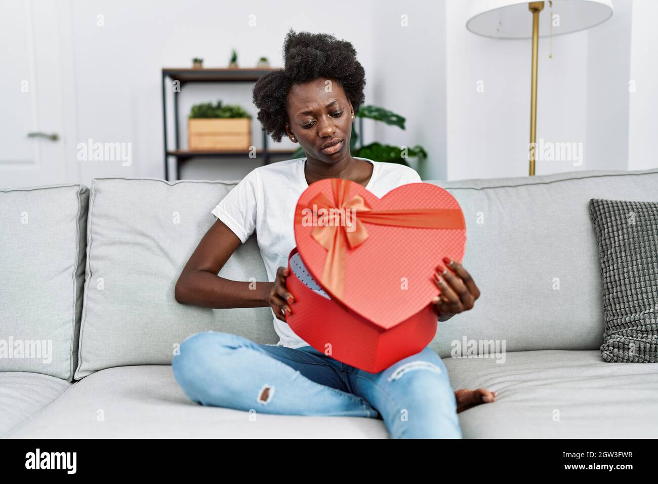 African young woman opening romantic gift depressed and worry for ...