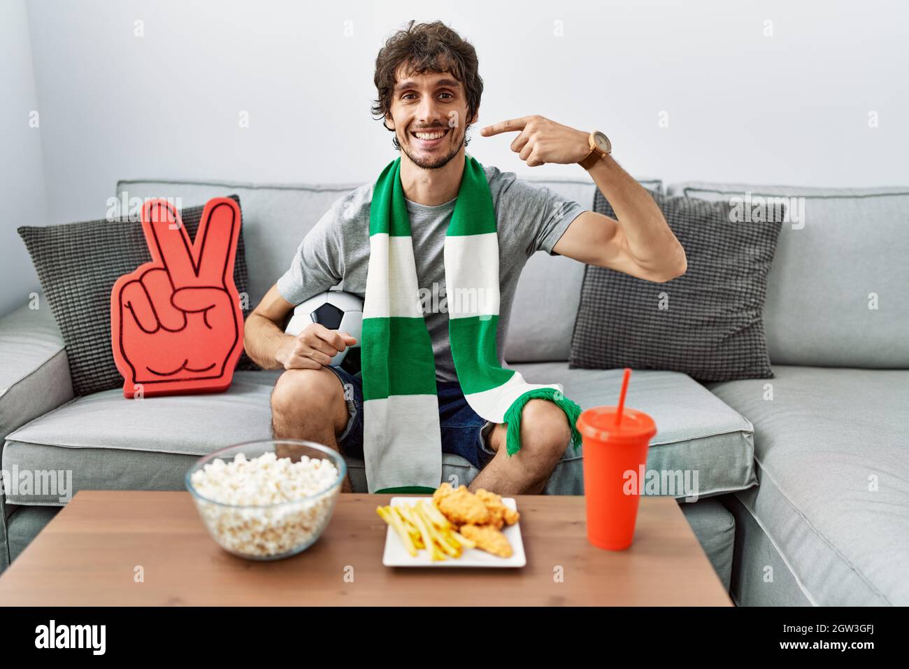 Young hispanic man football hooligan cheering game at home smiling ...