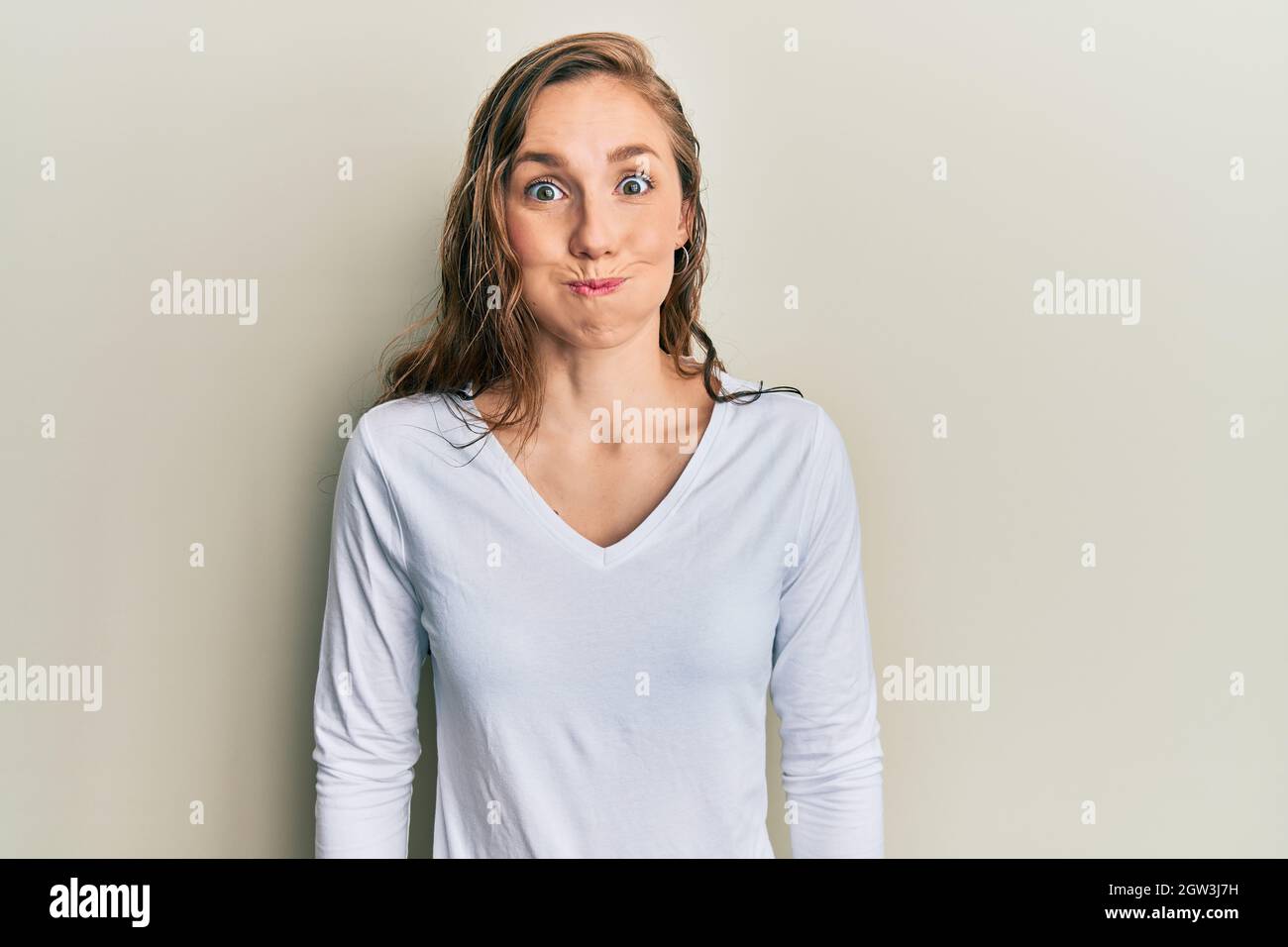 Young blonde woman wearing casual clothes puffing cheeks with funny ...