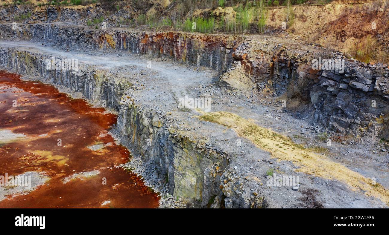 Large granite quarry with gray stone. Red water at the bottom of the ...