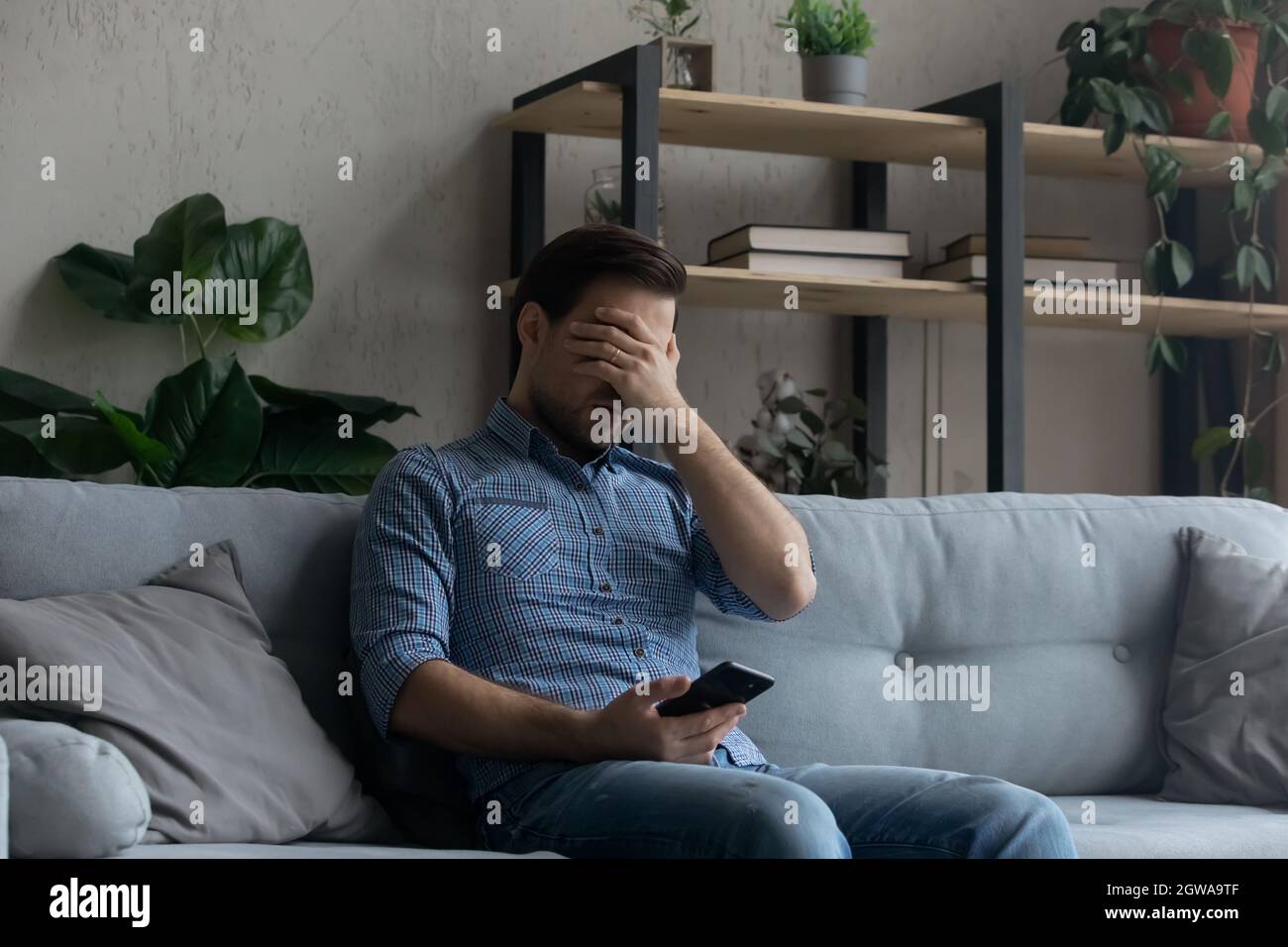 Frustrated young man covering face with hand, holding smartphone Stock ...