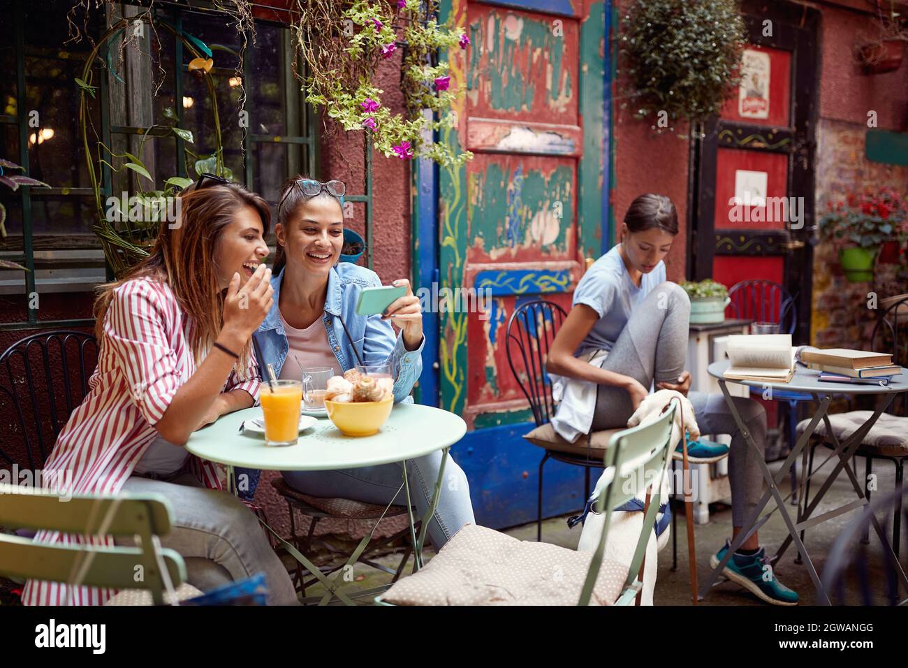 group of people in outdoor cafe. One female friend showing to another ...