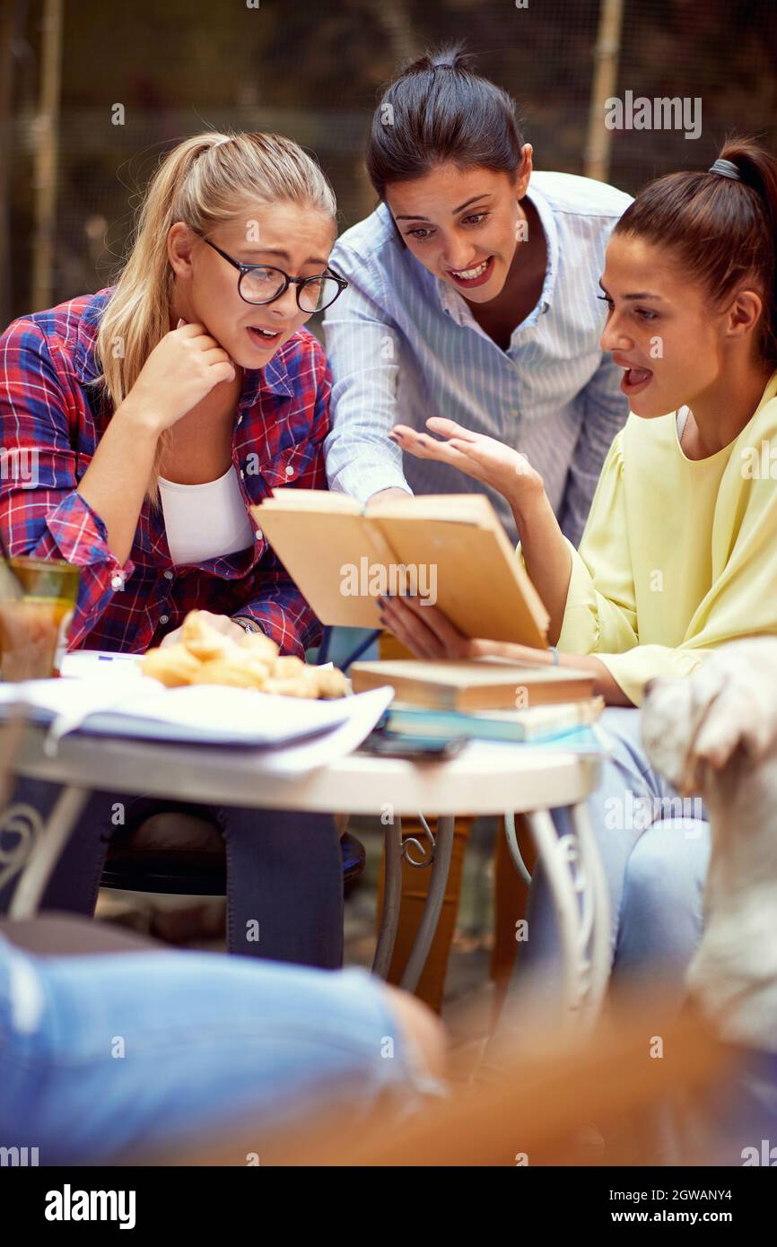 group of young caucasian females reading together in outdoor cafe ...