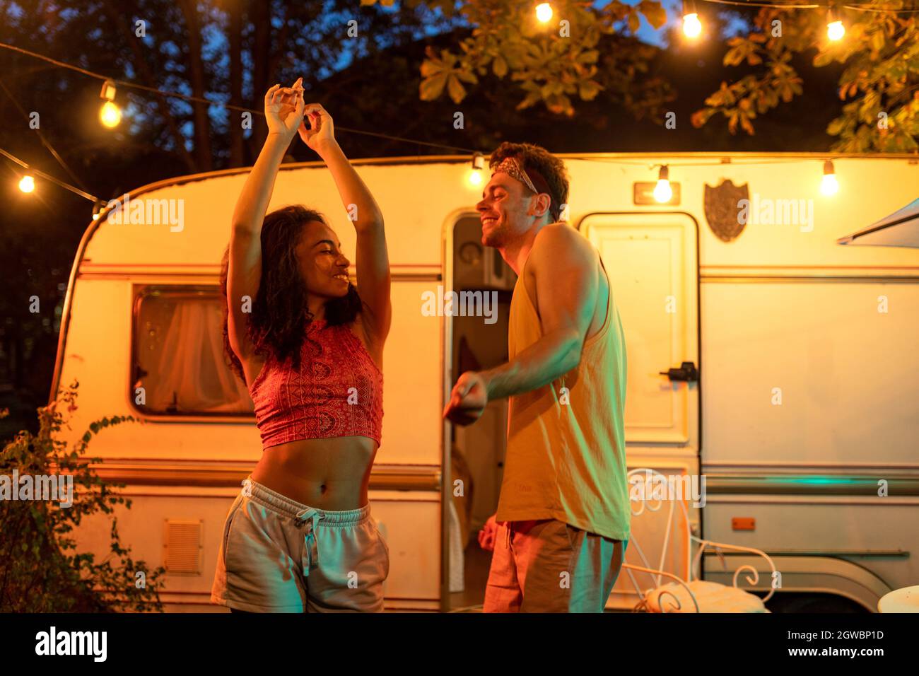Young couple on vacation with the camper. Dancing outdoor in the night ...