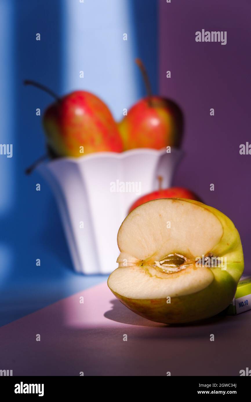A vertical, close-up shot of a cut apple and a bowl full of apples with ...