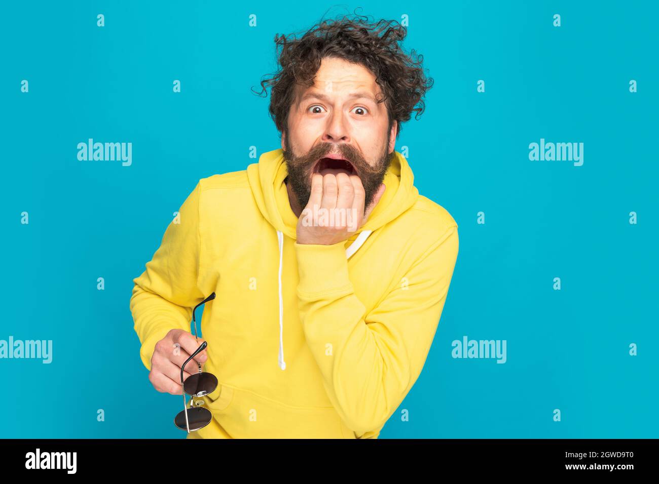 scared young man in yellow hoodie holding sunglasses, making an afraid ...