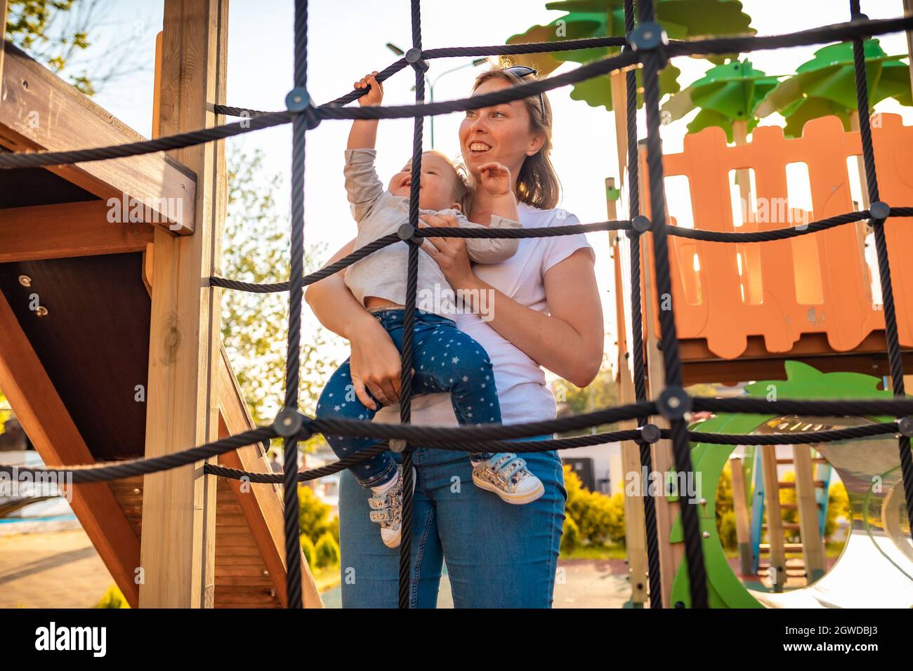 A young smiling caucasian mother plays with a baby on the playground ...