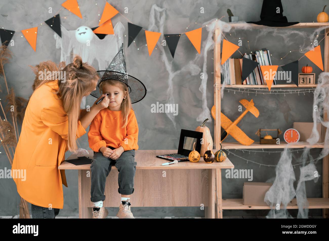 Woman and child getting ready for the Halloween holiday. Mom applies ...
