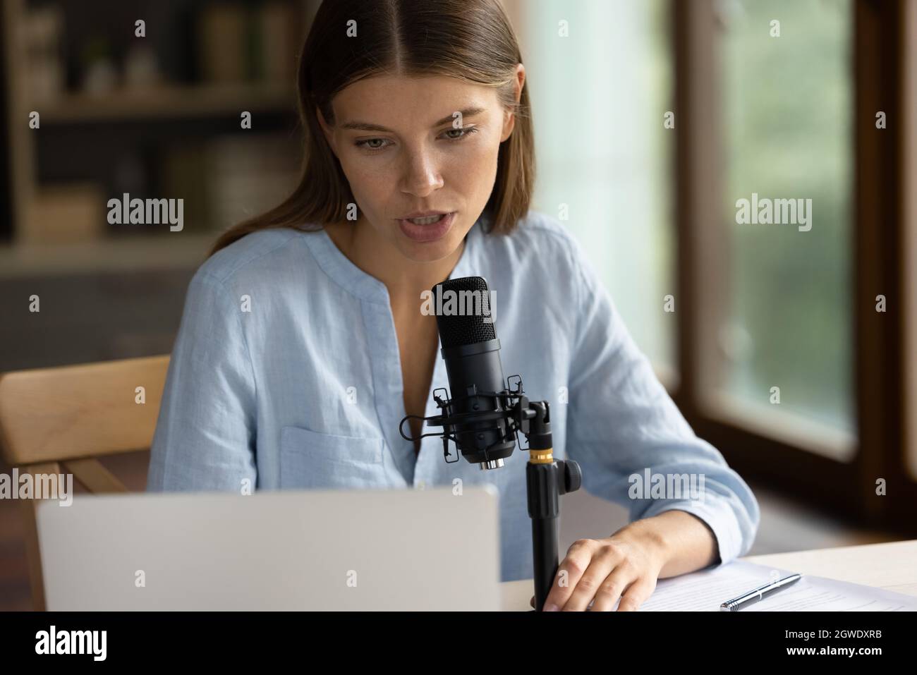 Serious young 20s millennial girl speaking at microphone at laptop ...