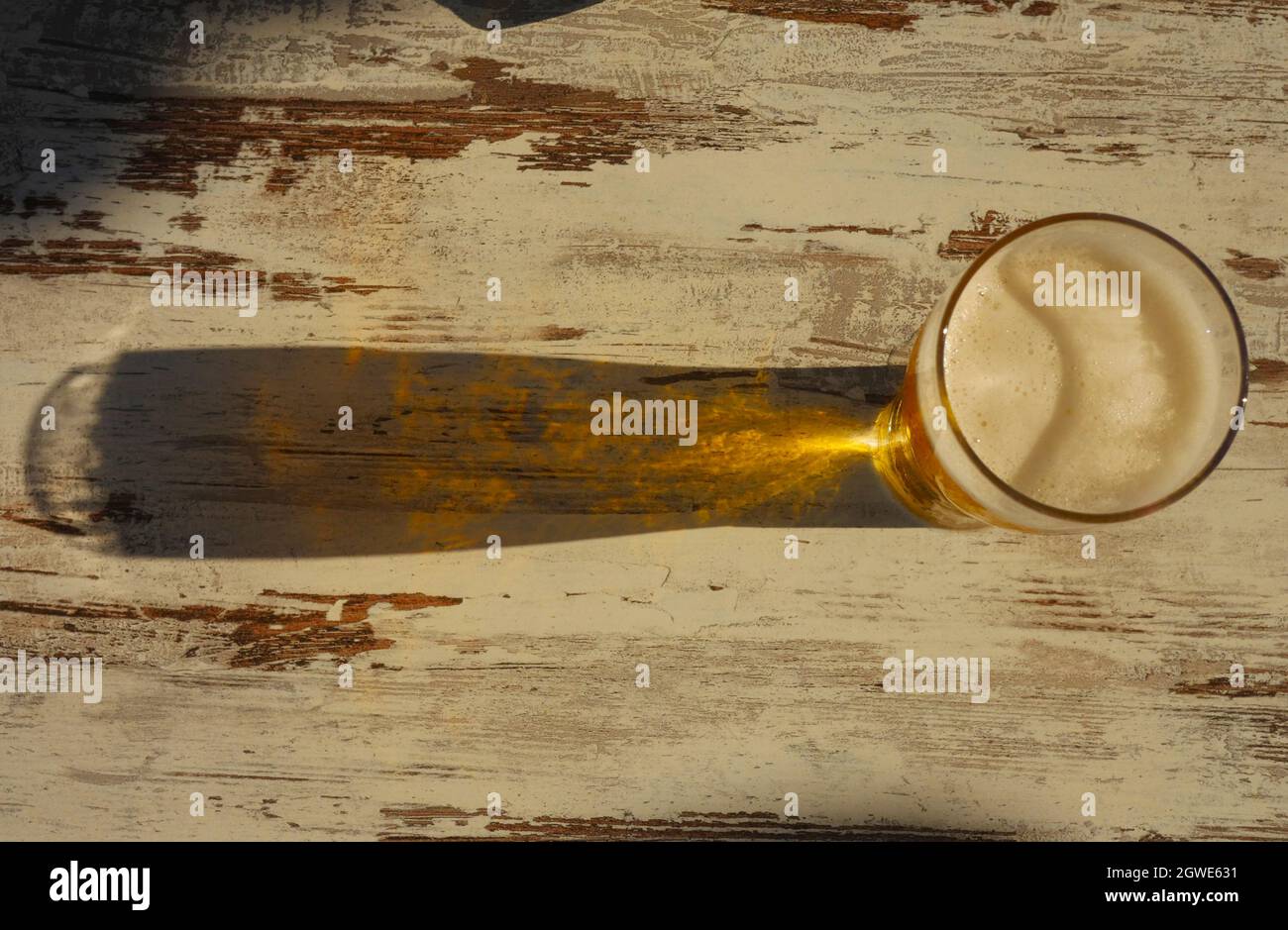 A pint of beer on a rustic table on the beach. The sun shines through ...