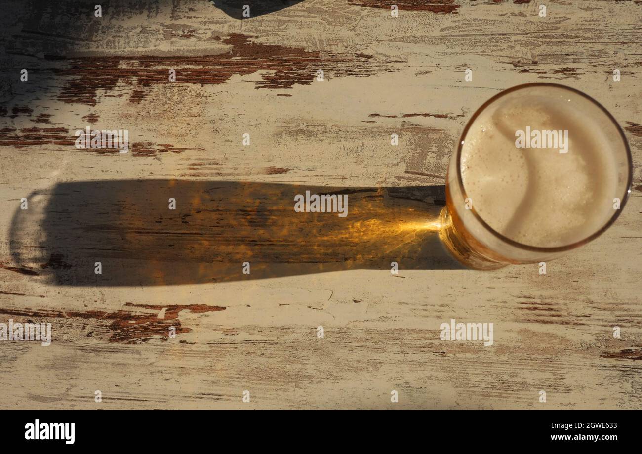 A pint of beer on a rustic table on the beach. The sun shines through ...
