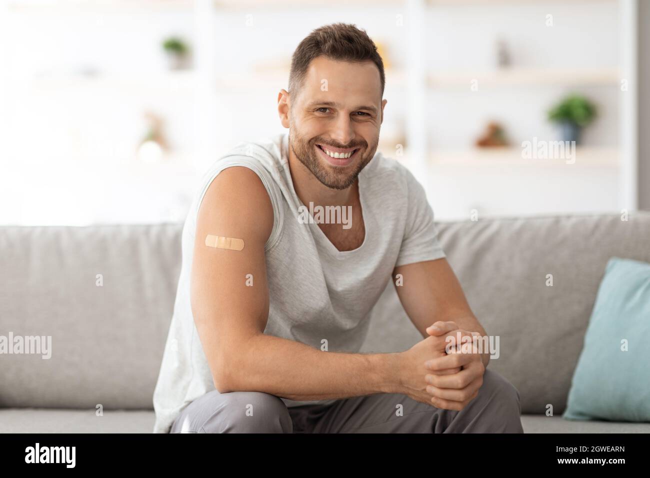 Coronavirus vaccination concept. Young healthy man sitting on sofa at ...