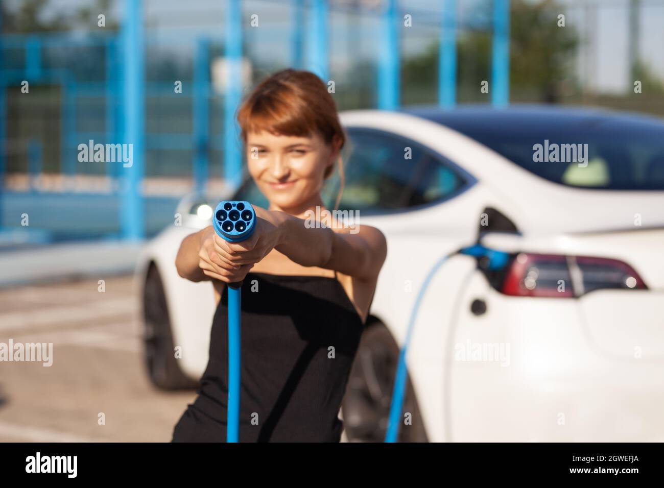 Beautiful young girl next to an electric car. Posing and holding a ...