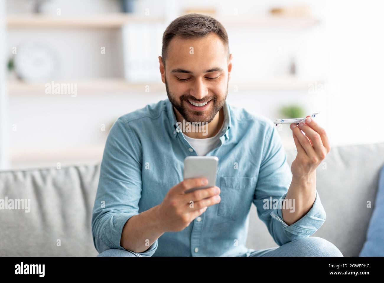 Happy young Caucasian guy holding toy plane, booking tickets or hotel ...
